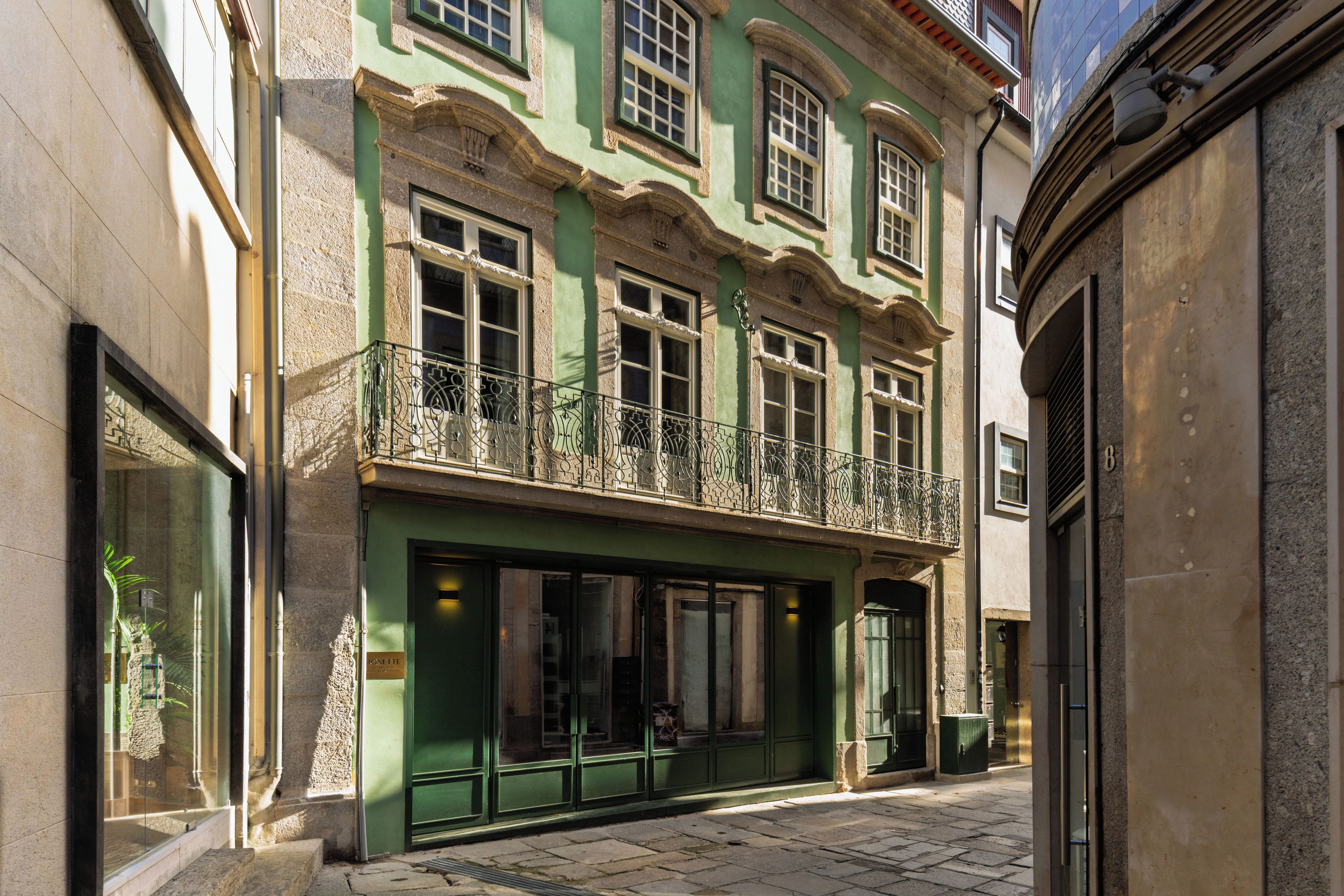 Um edifício com fachada verde, janelas amplas e uma varanda com grades de metal ornamentadas.