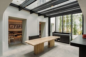 Decoração moderna com uma mesa de madeira central, área de estar com cadeiras e vista para o verde através de grandes janelas.