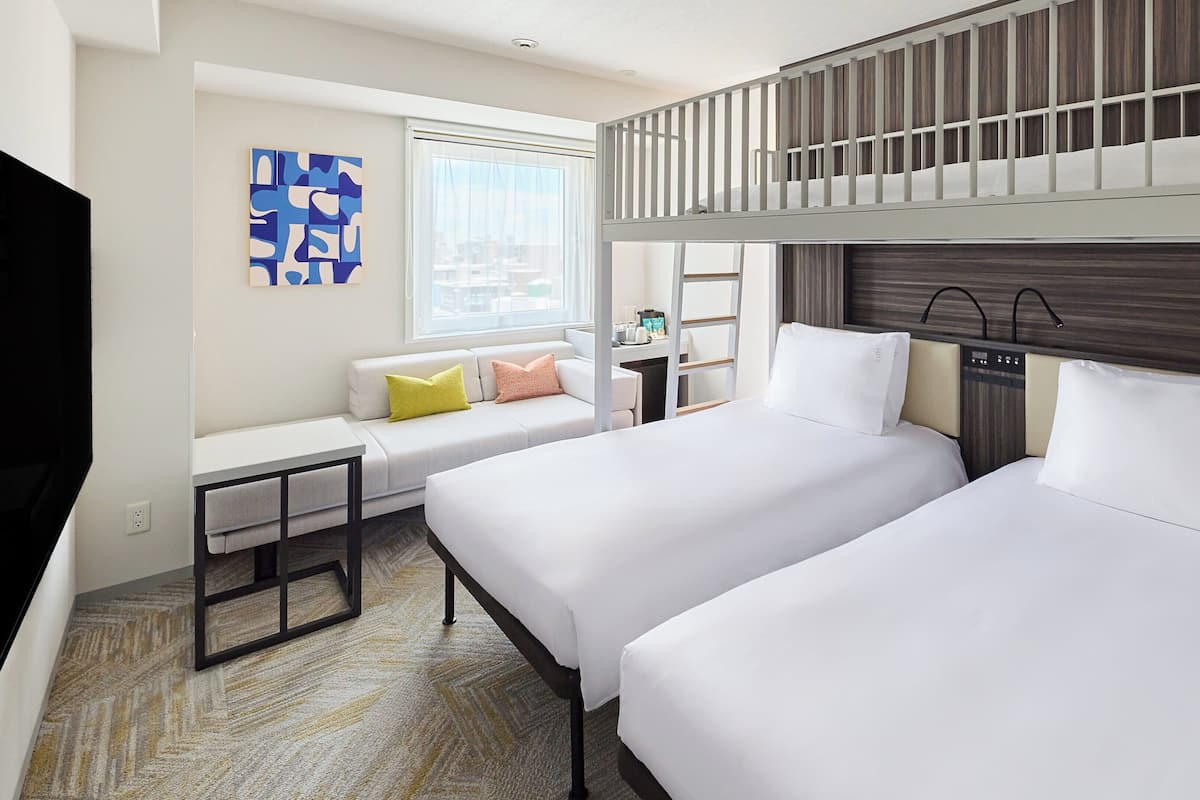 Quarto de hotel com duas camas, um sofá, uma escrivaninha e uma televisão.