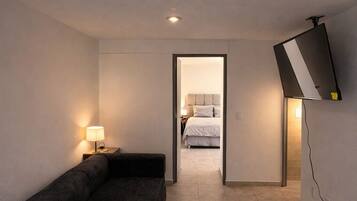 Quarto de hotel moderno com sofá, cama, televisão na parede e uma mesinha com abajur.