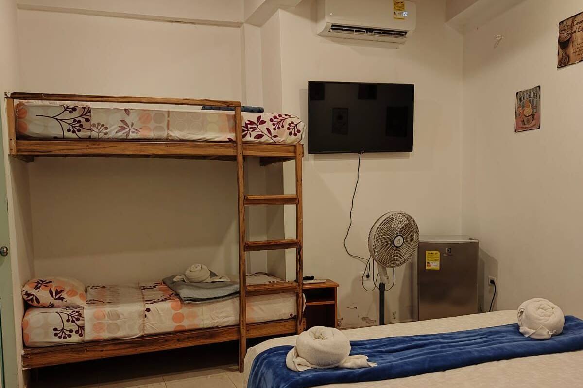 Quarto com beliche, cama individual, televisão, ar condicionado e ventoinha.