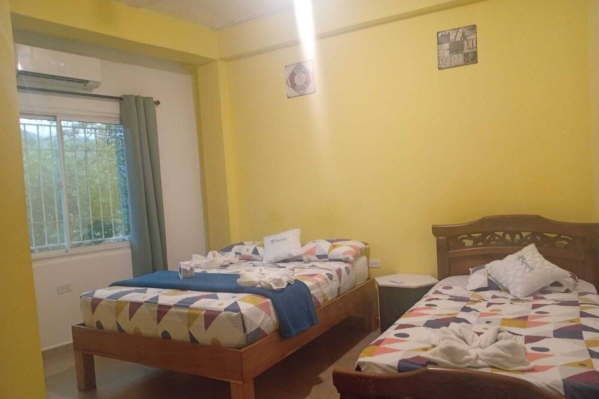 Quarto com duas camas, janela com cortinas e ar-condicionado na parede.