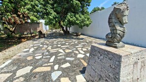 Um pátio com piso em mosaico, uma escultura de pedra e árvores.