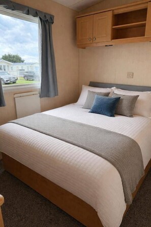 Quarto com cama, janela com cortinas, armário de madeira sobre a cama e vista para o exterior.