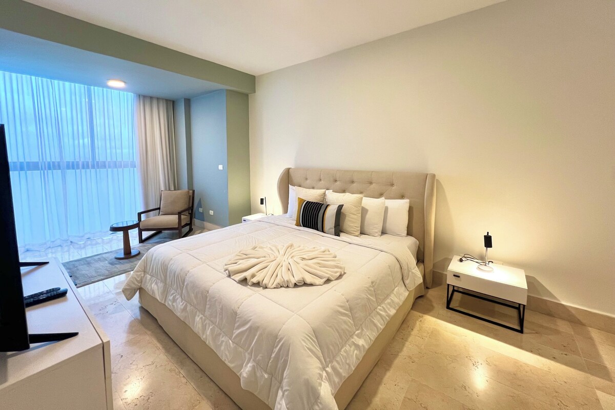 Quarto com uma cama grande, uma cadeira, uma TV e uma mesa de cabeceira com abajur.