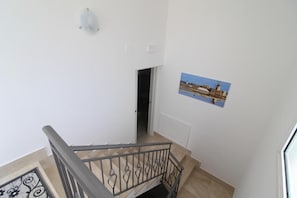 Escada com corrimão de metal, luminária fixada na parede e quadro com imagem de um edifício.