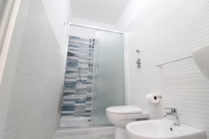 Uma casa de banho moderna com cabine de duche em vidro, sanita branca e lavatório com espelho.