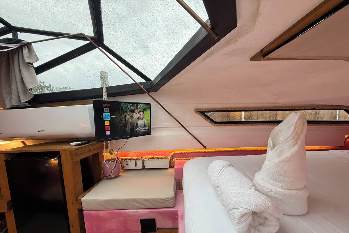 Um quarto aconchegante com uma cama, televisão, uma mesa pequena e uma janela.