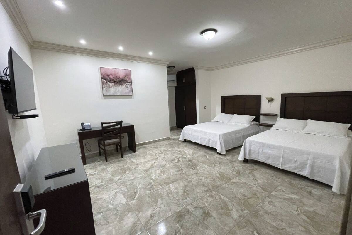 Quarto de hotel com duas camas, uma escrivaninha, uma cadeira, uma televisão e um quadro na parede.