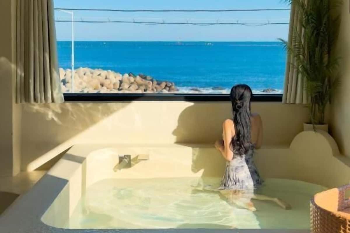 Quarto com uma grande janela com vista para o mar, uma banheira e uma cadeira de vime.