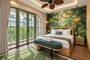 Quarto de hotel com uma grande porta de vidro deslizante para uma varanda, uma cama com cabeceira estofada em verde e um mural com tema tropical na parede.