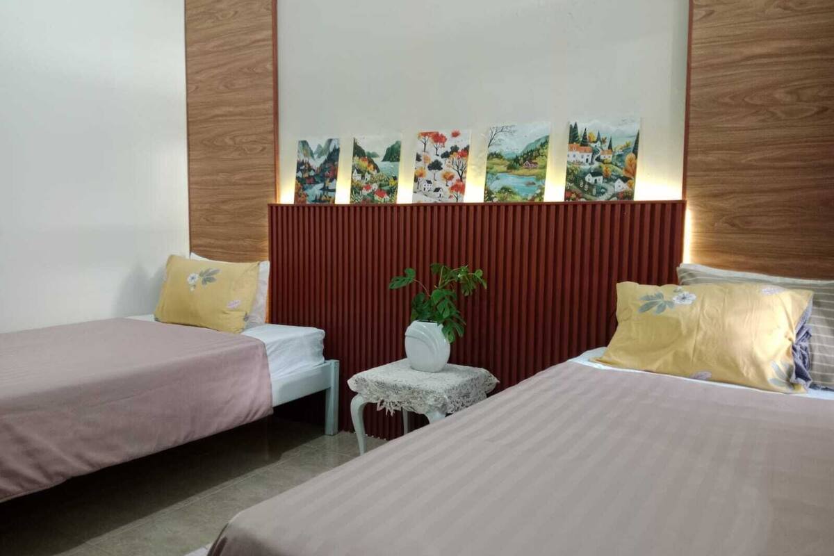 Quarto com duas camas, uma mesinha com uma planta e uma parede decorada com obras de arte.