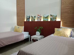 Quarto com duas camas, uma mesinha com uma planta e uma parede decorada com obras de arte.