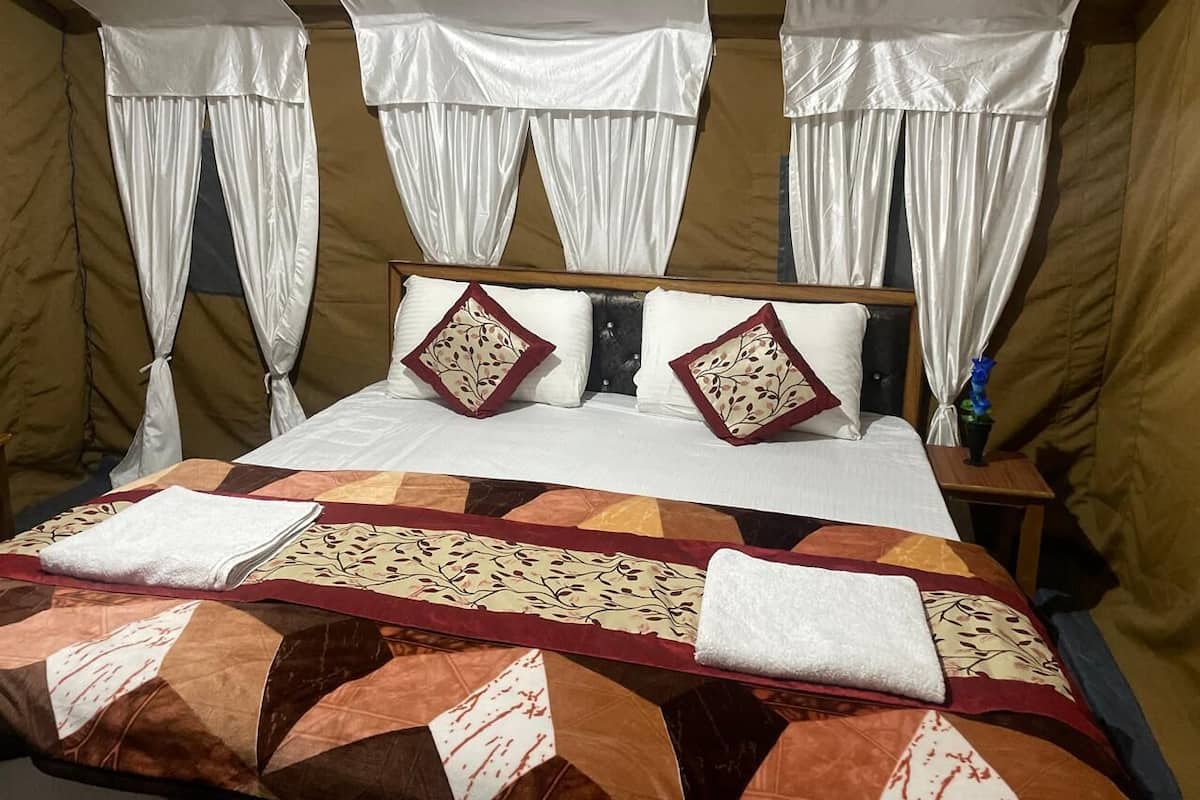 Cama com lençóis brancos, duas almofadas decorativas, um edredom e toalhas brancas.