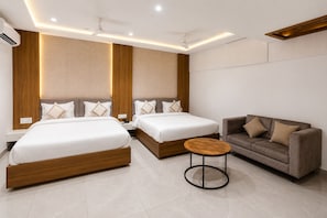 Quarto de hotel com duas camas, um sofá, uma mesa de centro redonda e um ventilador de teto.