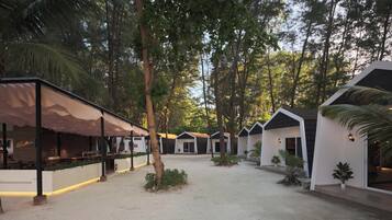Fileira de cabanas modernas, com telhados brancos, área de estar coberta ao ar livre e um pátio de areia.