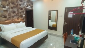Quarto de hotel com cama, escrivaninha com chaleira, espelho e ventilador de teto.