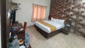 Quarto de hotel com cama, escrivaninha com computador, cadeira, guarda-roupa, espelho, ventoinha no teto e parede com desenho estampado.