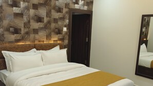 Cama com roupa de cama branca e um cobertor amarelo mostarda, cabeceira de madeira e parede com padrão geométrico.