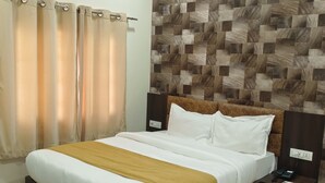 Quarto de hotel com cama, cortinas, parede com padrão geométrico, luminária no teto e mesa de cabeceira com telefone.