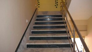 Uma escadaria com degraus pretos e guarda-corpo de metal, que leva a um andar superior.