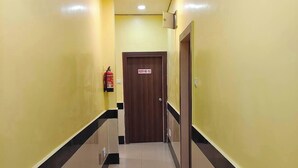 Um corredor com um extintor de incêndio, uma porta com a inscrição 'ROOM NO-102' e um acessório de iluminação no teto.