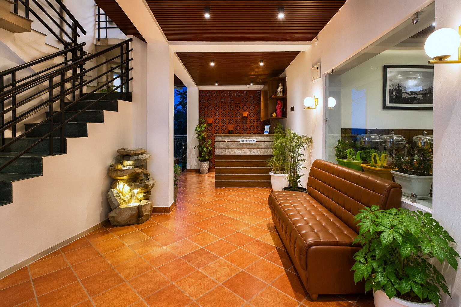 Uma área de recepção com escada, balcão de atendimento, sofá de couro marrom e plantas em vasos.