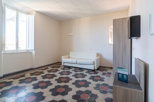 Quarto com sofá branco, piso estampado, televisão de tela plana e painel de madeira na parede.