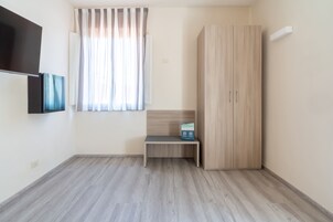 Um quarto com guarda-roupa de madeira, um banco e uma janela com cortinas.