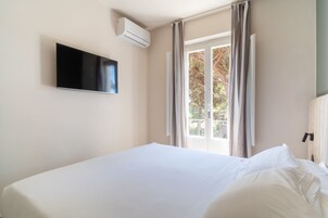 Quarto de hotel com cama, televisão de tela plana na parede e janela com cortinas.