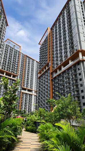 Um edifício residencial alto com várias varandas, cercado por vegetação exuberante e um caminho pavimentado.