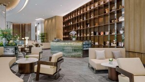 Um lobby moderno com áreas de estar, balcão de recepção e uma grande estante com objetos decorativos.