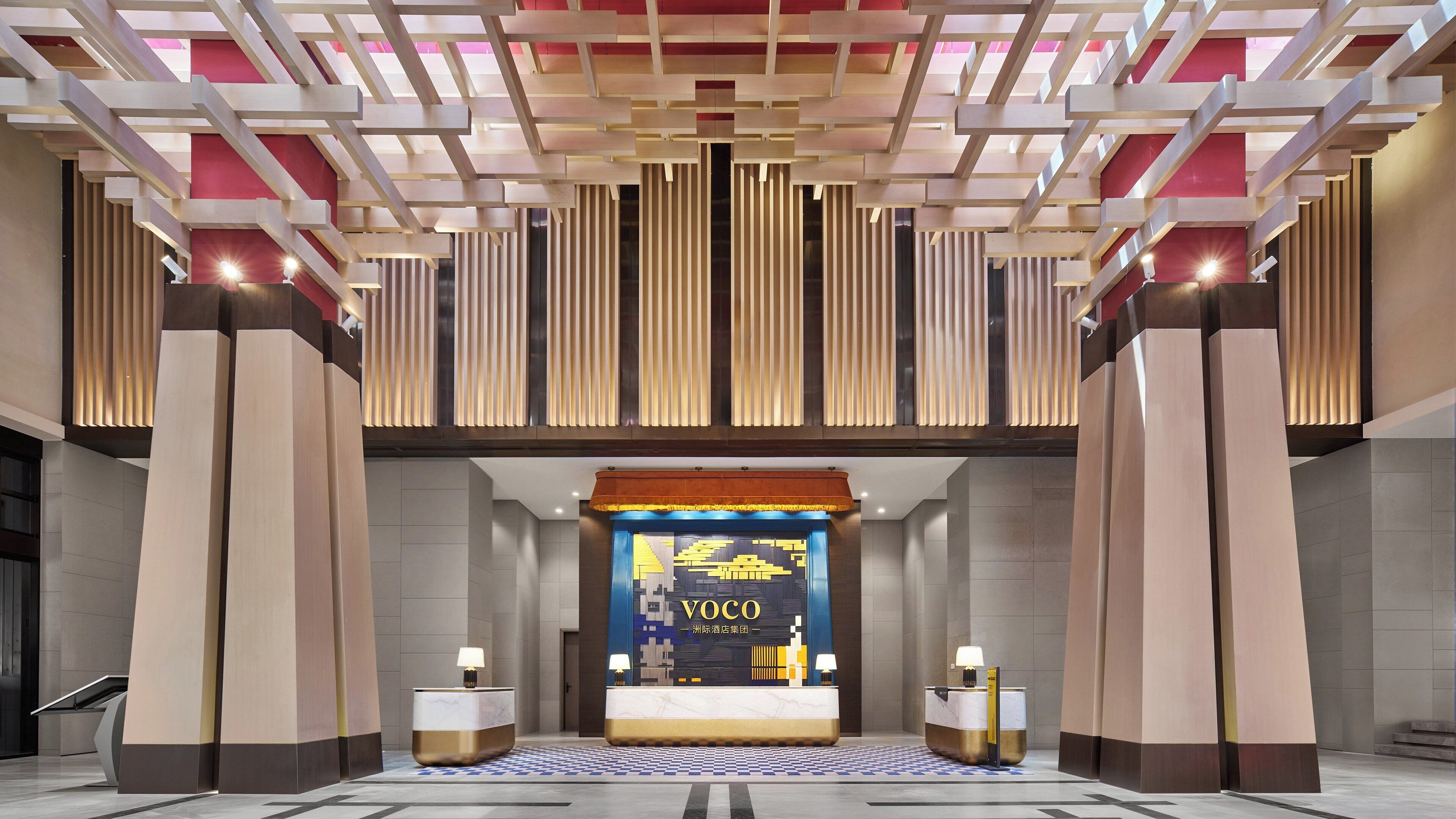 Uma área de recepção de hotel com design moderno, destacando um balcão de atendimento, duas luminárias e um display digital.