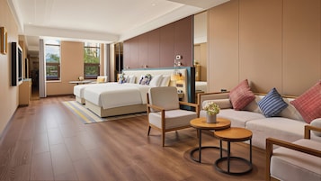 Quarto de hotel com uma cama grande, um sofá, uma poltrona, uma mesinha e uma televisão.