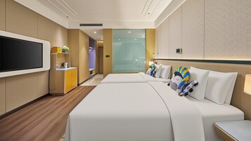 Quarto de hotel com uma televisão de tela plana grande, um minibar, uma cama com almofadas decorativas e vista para o corredor.