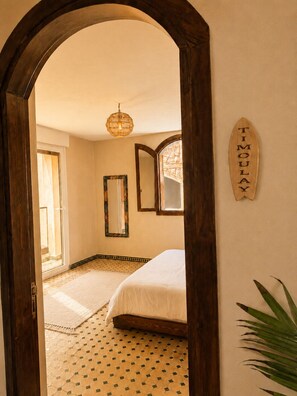 Quarto com cama, espelho, placa de madeira e porta que dá para outro cômodo.