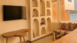 Um quarto com uma grande mesa de madeira, uma TV fixada na parede e uma estante embutida com vários compartimentos.