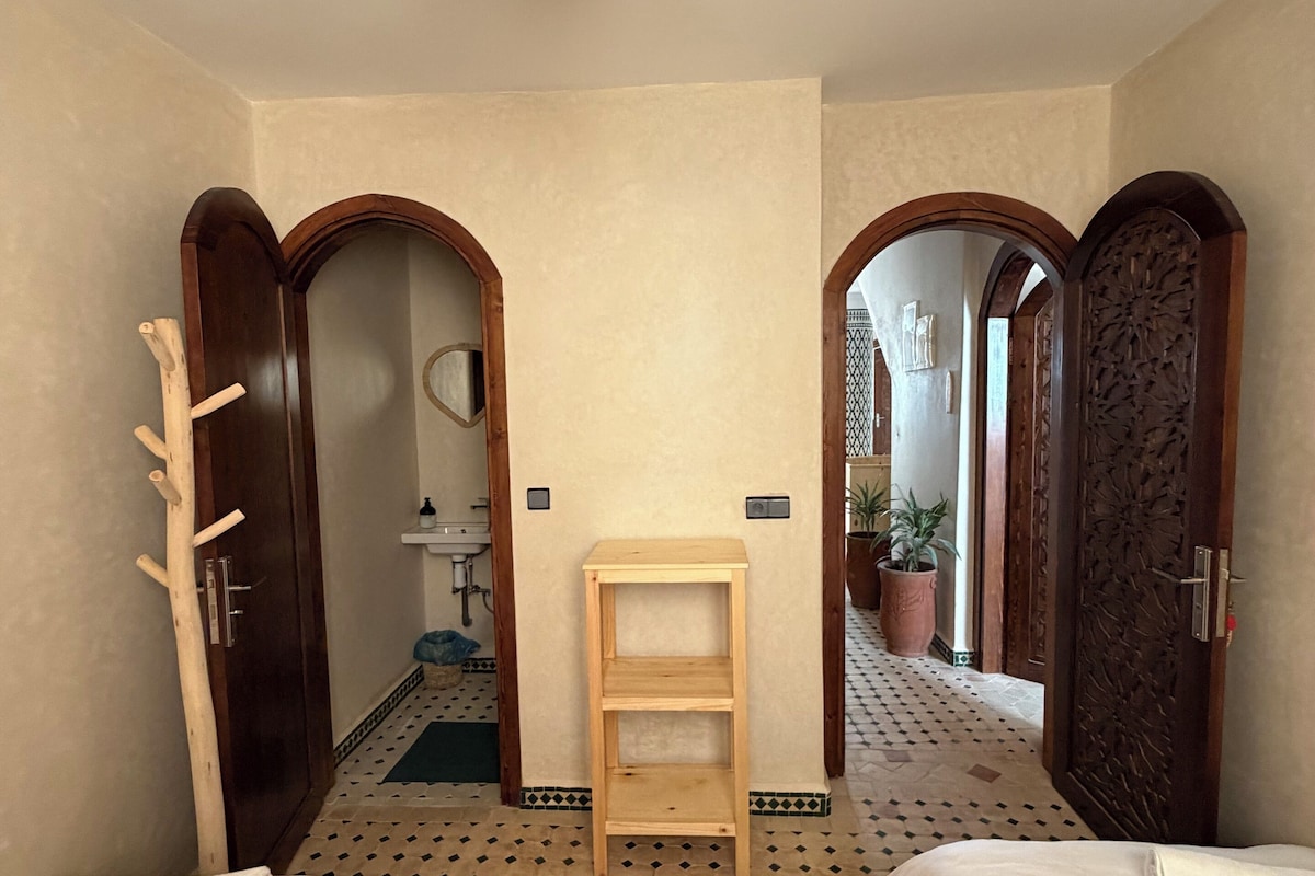 Quarto com duas camas, uma estante de madeira, luminária pendente e piso estampado.