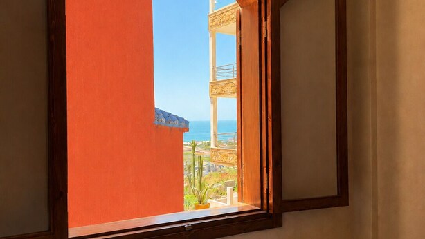 Um quarto com uma cama, uma janela com arco e vista para um edifício e um corpo de água.