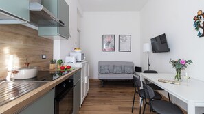 Uma cozinha compacta com eletrodomésticos modernos, uma sala de jantar com sofá e uma televisão de tela plana na parede.