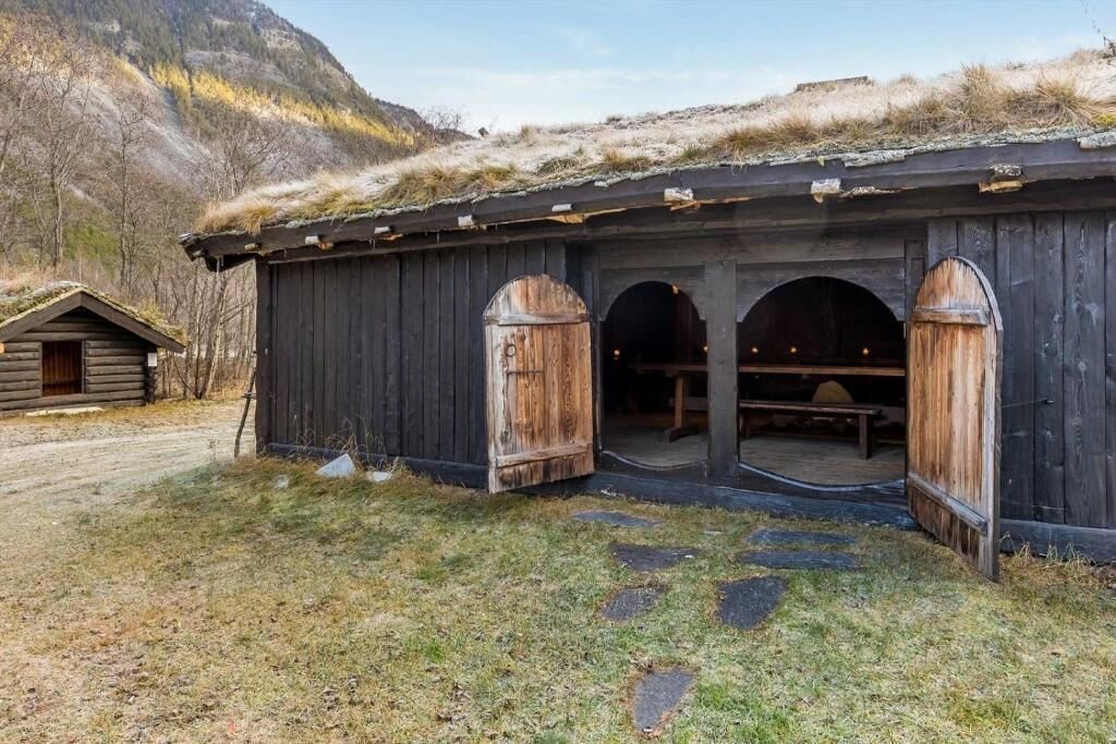 Um edifício rústico de madeira com telhado de palha, duas portas em arco e um banco no interior.