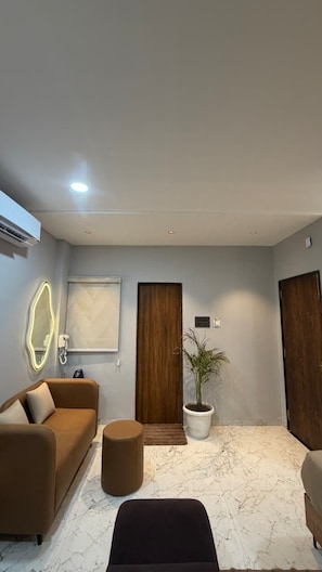 Uma sala de estar moderna com sofá, banqueta, planta em vaso e uma porta de madeira.