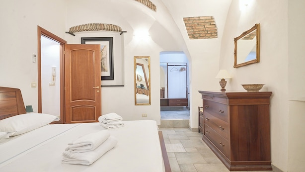 Quarto de hotel com uma cama, cômoda de madeira, espelho e porta que dá para outro quarto.