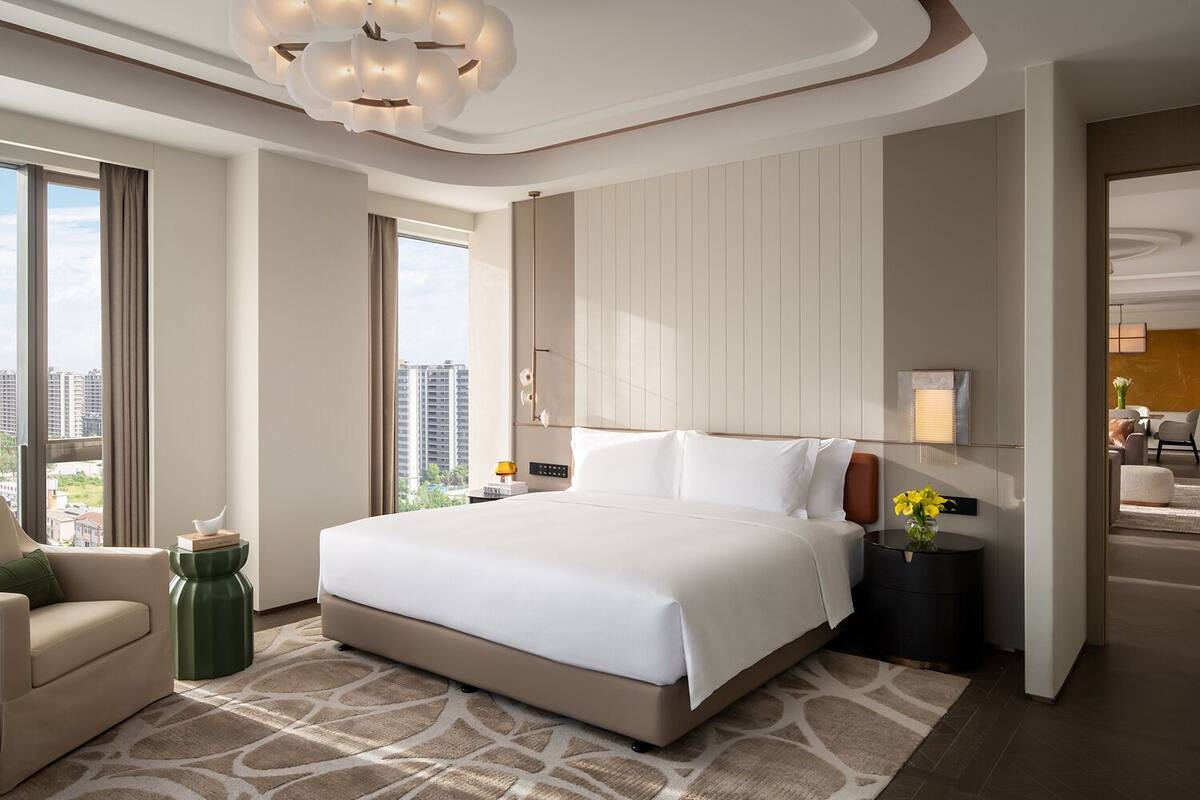 Quarto de hotel moderno com uma cama grande, vista para a cidade e área de refeições.