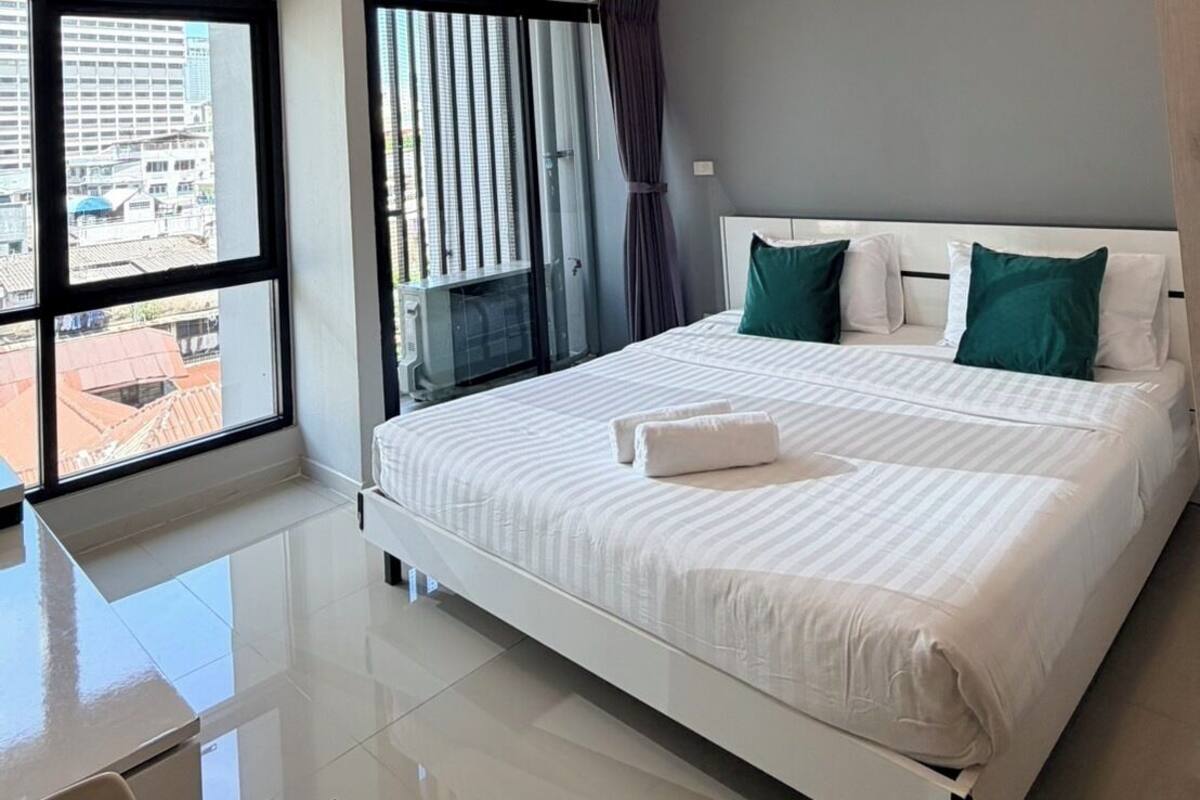 Quarto de hotel moderno com uma cama grande, uma janela com vista para edifícios, ar condicionado e uma luminária de teto.