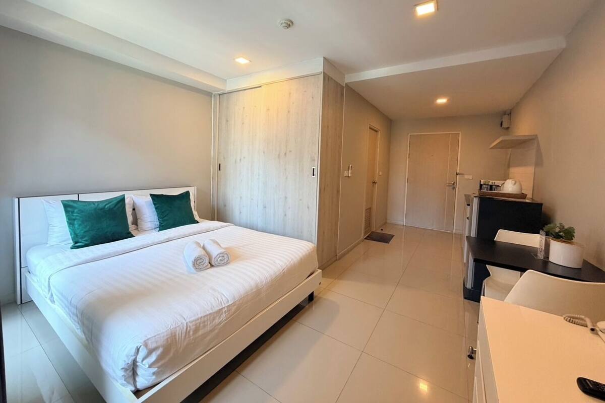 Quarto de hotel com cama, escrivaninha, cadeira e uma pequena cozinha.