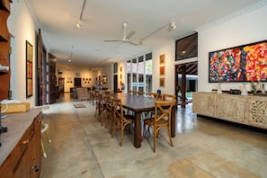 Uma sala de jantar espaçosa com uma grande mesa de madeira e cadeiras, um ventilador de teto e um armário decorativo com uma pintura floral.