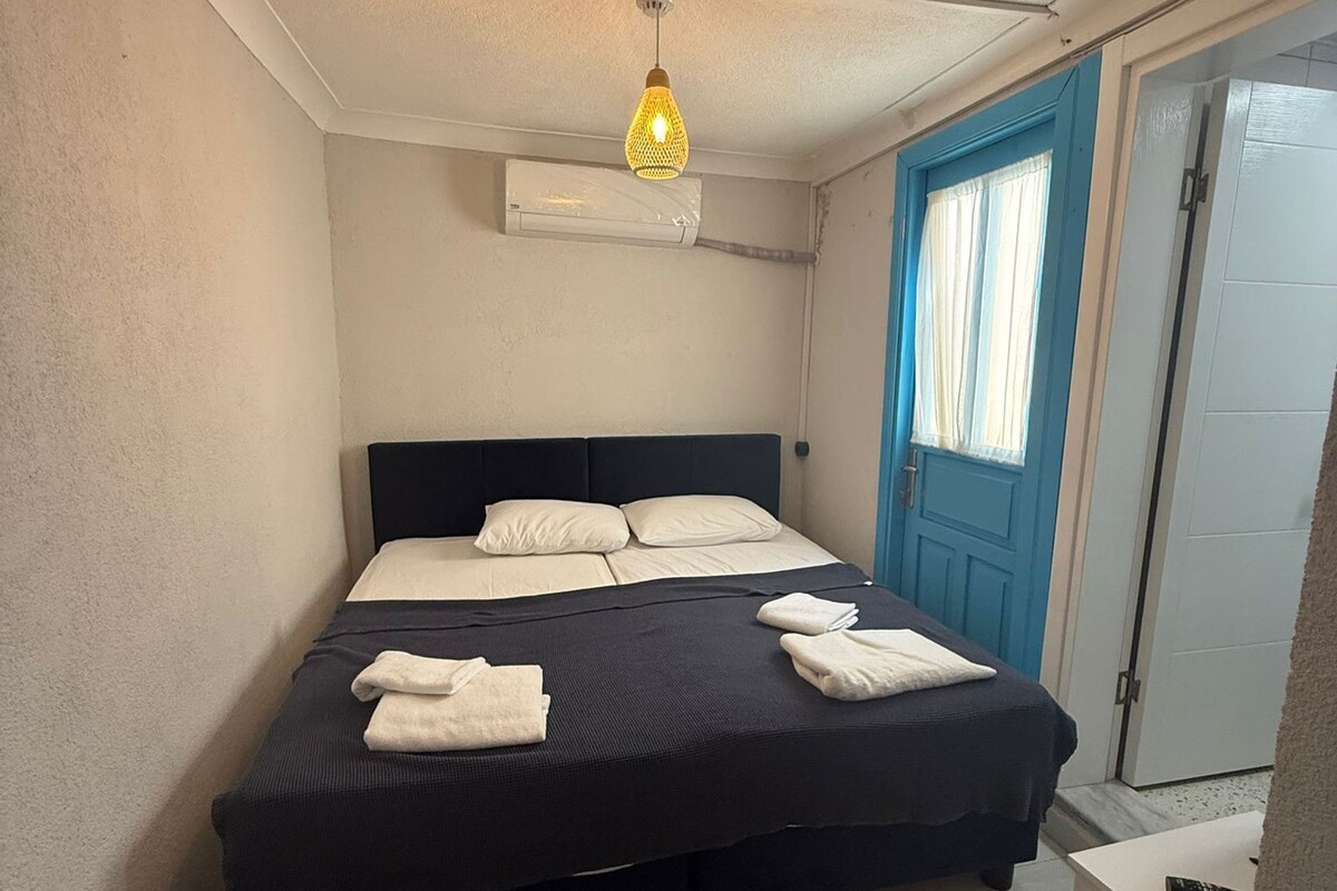 Quarto com cama, luminária no teto, janela com cortinas e banheiro com vaso sanitário e pia.