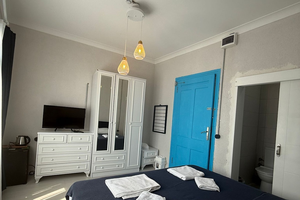 Quarto com cama, guarda-roupa, televisão e porta azul.