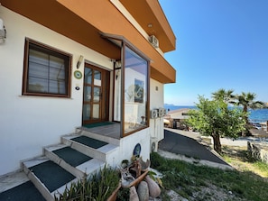 Um edifício com uma grande porta de vidro, degraus que levam a um alpendre e vista para o mar.